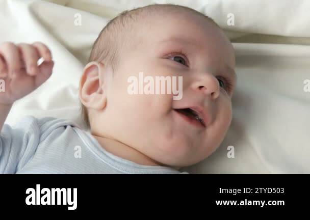 A two month old happy newborn baby lies on the bed and experiences ...