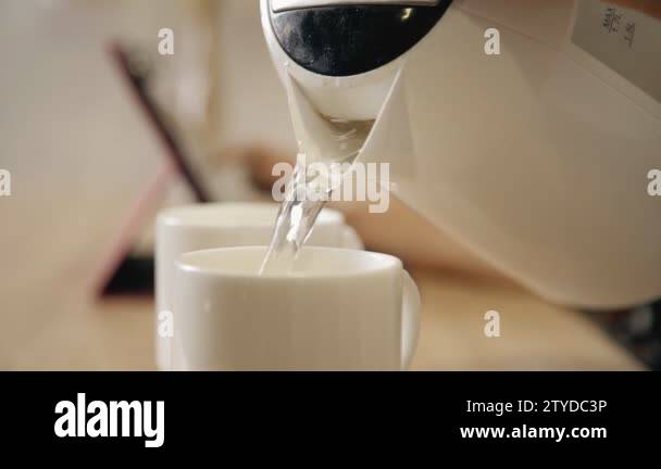 Hot boiled water pouring to mugs from electric pot. Tea maker making ...