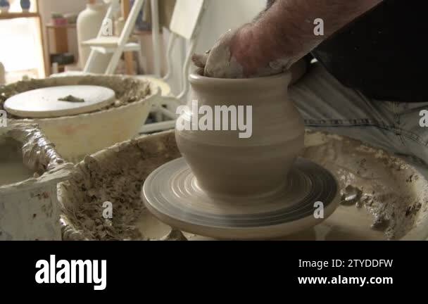 Potter craftsman molding the neck and mouth of a new piece in mud in ...