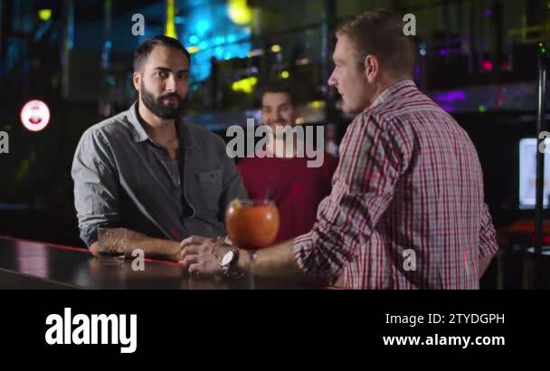 Young smiling Caucasian man coming to fellows in night club and ...