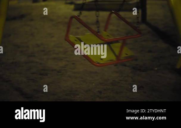Swing on the playground at night, no one in the park. Close-up rides in ...