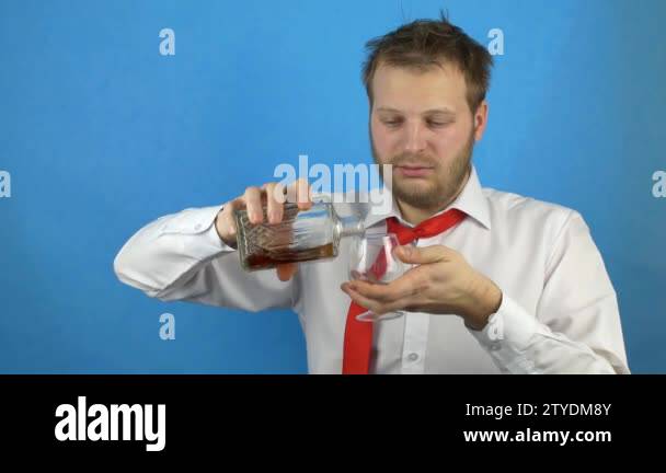Drunk man alcoholic with a beard in a white shirt and tie pours alcohol ...