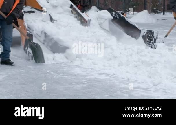People with shovels and tractor clean the street from the snow. Cleaning after a snow storm ...
