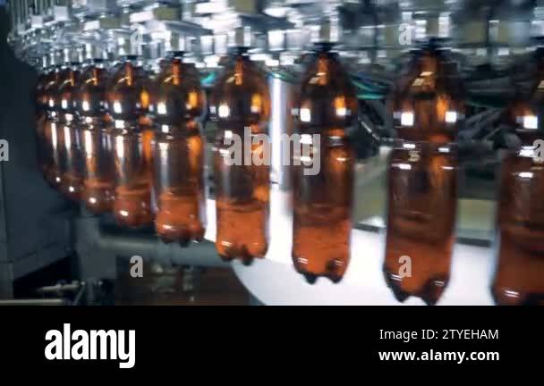 Beer is pouring into rotating plastic bottles from a factory machine ...