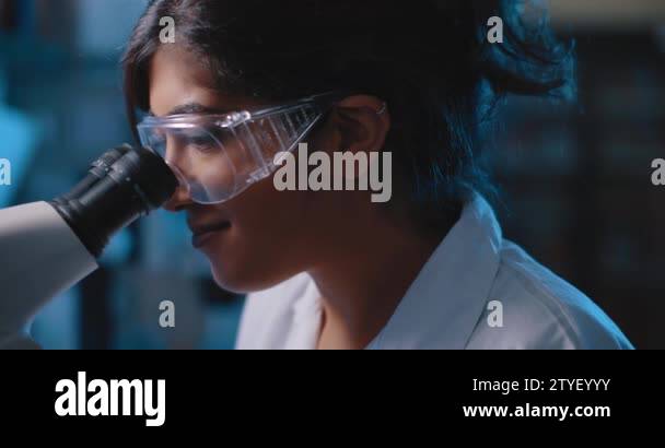 Female research scientist looking into microscope, wearing safety ...