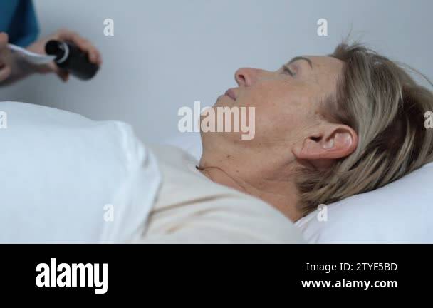 Nurse giving syrup to elderly female patient lying in bed, hospital ...