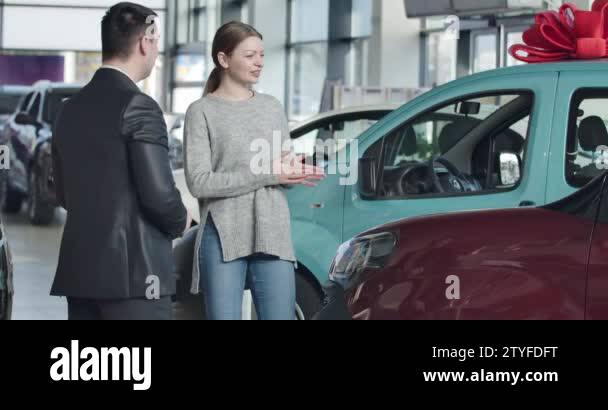 Caucasian dealer consulting young beautiful woman in car dealership ...