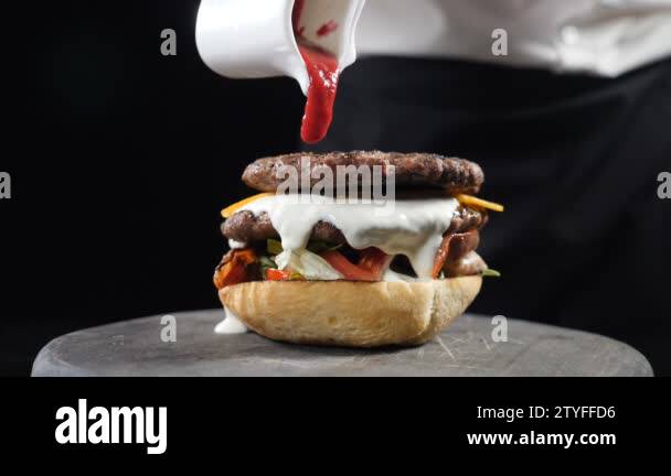 Chef preparing juicy burger and pours spicy sauce on it making burgers ...