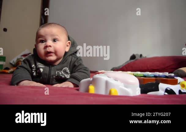 cute four months old baby boy having tummy time on red bed cover and ...