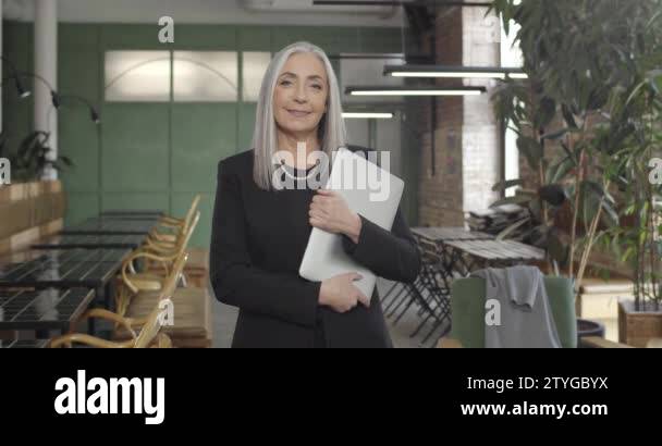 Grey haired female boss standing in modern coworking zone and holding ...