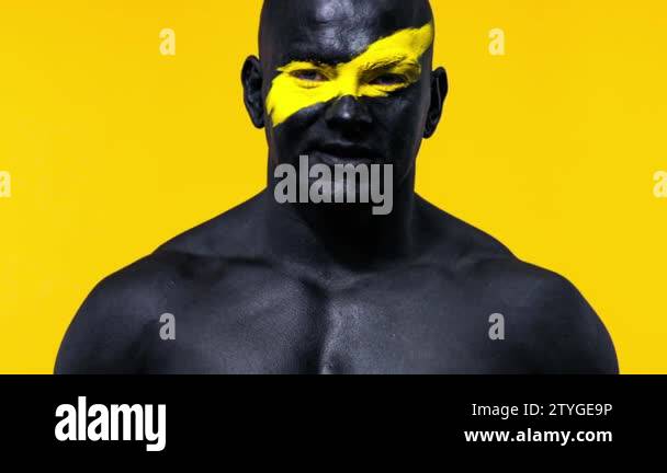 Man bodybuilder athlete with yellow color on face art and black body ...