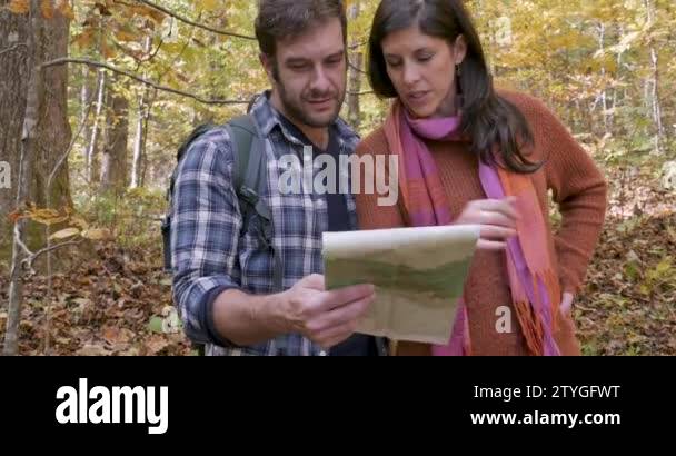 Couple lost in the woods looking at a paper map and talking about their ...