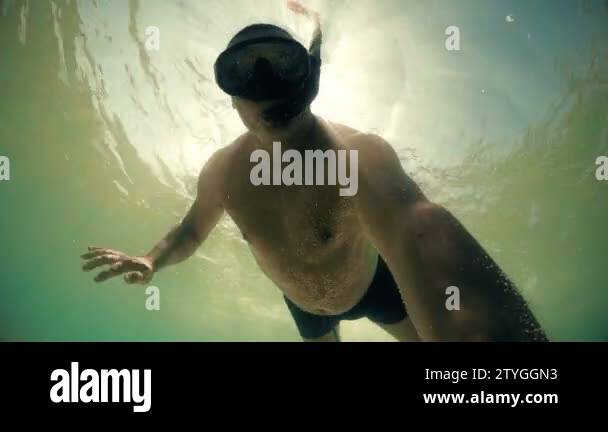 Greetings by diver with snorkel mask waving hand underwater backlit by ...