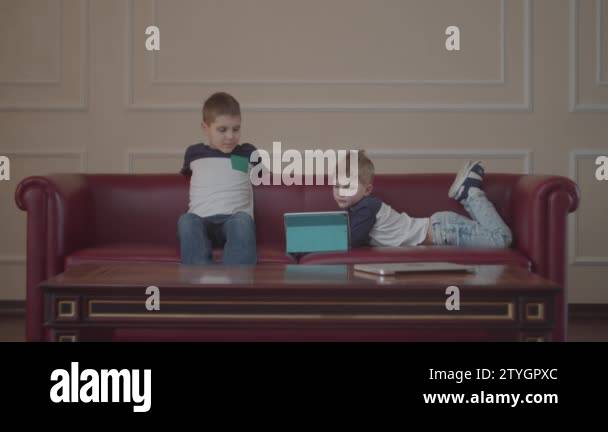 Two brothers in the same clothes using gadgets on home couch. Siblings ...