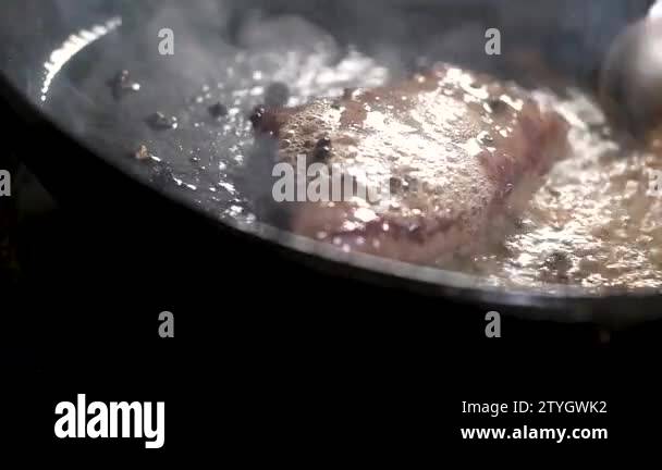 cook pouring boiling oil on fried steak. Oil flows down on a hot frying ...