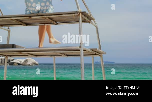 Rear view of woman sitting on observation tower on the beach. She is ...
