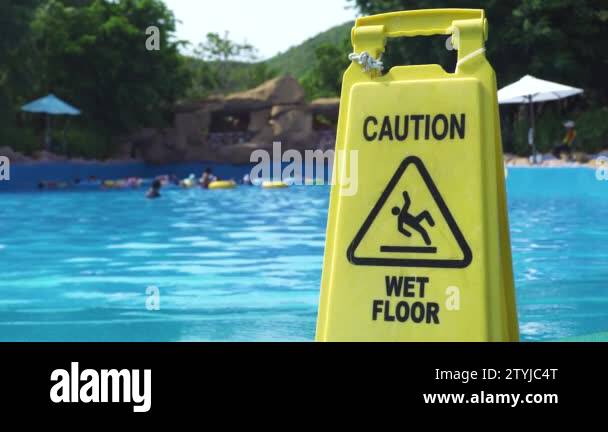 Yellow wet floor caution sign on swimming pool background in amusement ...