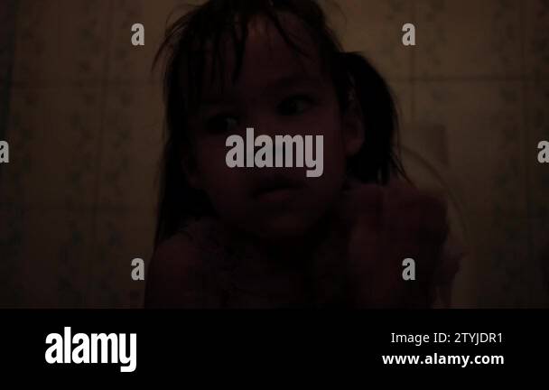 Cute little girl feel scared while sitting on the toilet bowl with broken flickering fluorescent ...