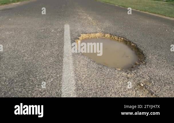 LOW ANGLE, CLOSE UP: Large gaping pothole filled with muddy water ...