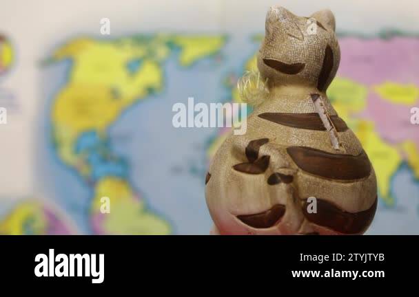 Ceramic piggy bank stands on a background of a world map. A man takes a ...