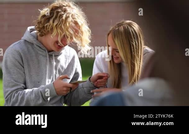 Teenage boy and girl sharing headphones sitting in grass as they hang ...