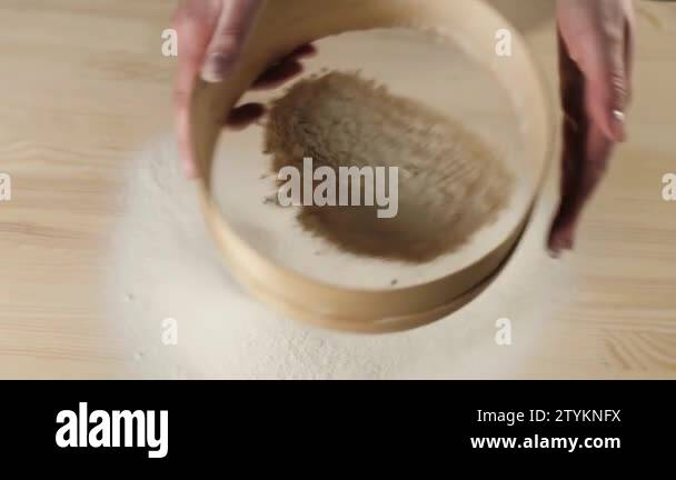 Professional baker hands sift flour through a wooden sieve on the table ...