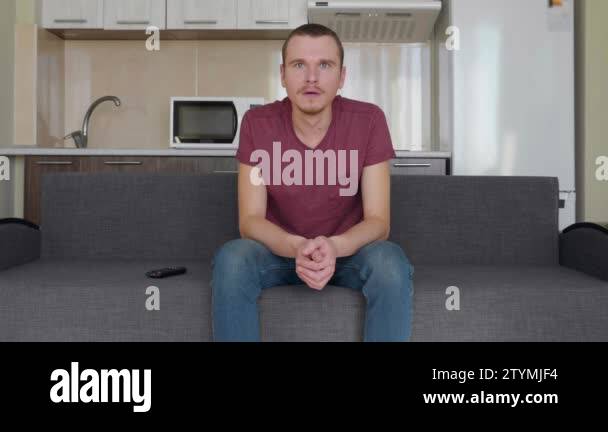 A man is watching TV. The young guy is sitting on the couch, opening ...