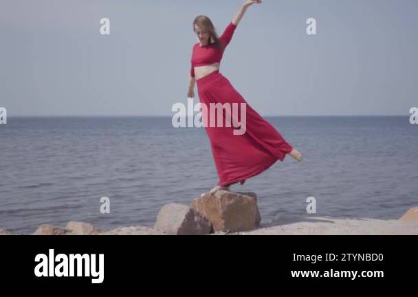 Graseful cute young woman in red long dress dancing raises hands on the ...