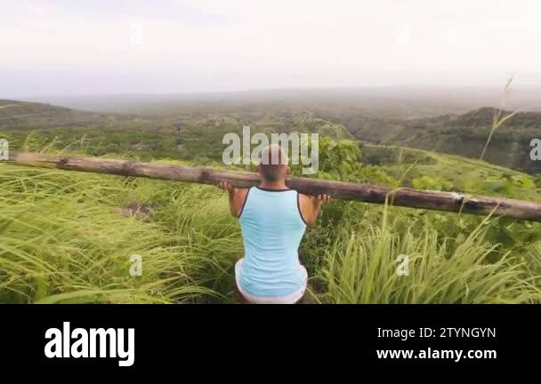 Man bodybuilder squatting with wooden barbell while outdoor training in ...