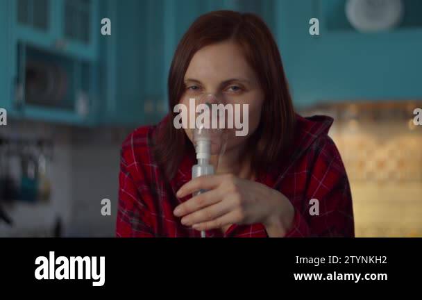 Young 30s woman in red shirt using inhaler for therapy of disease like ...