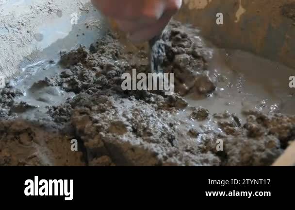 Male builder making cement. Blends cement clay and water, mixing all it ...