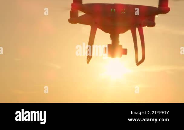 CLOSE UP LENS FLARE SILHOUETTE Small filming drone flying over golden ...