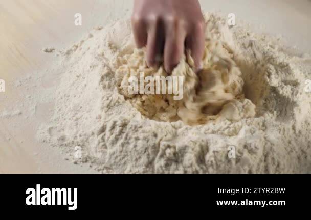 Professional baker begins to mix flour with egg in a deepening in a ...