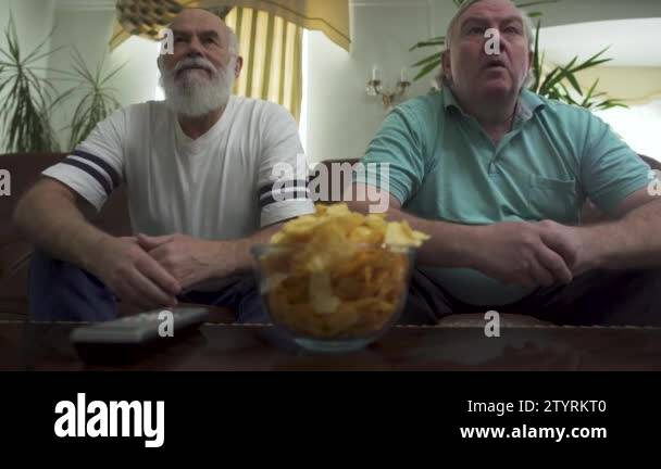 Two mature senior men sitting on the brown leather sofa watching TV ...