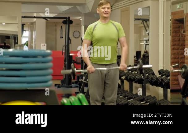 A overweight man lifts an ez barbell while standing at the gym ...