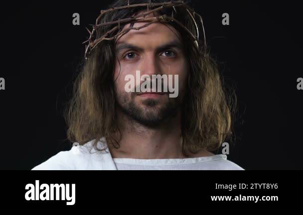 Crying Jesus Christ in crown if thorns looking at camera against dark ...