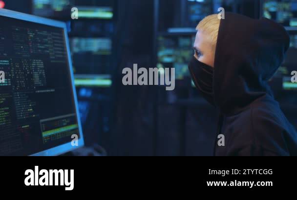 Side view on Caucasian woman with masked face and in hood working in cyber security center and ...