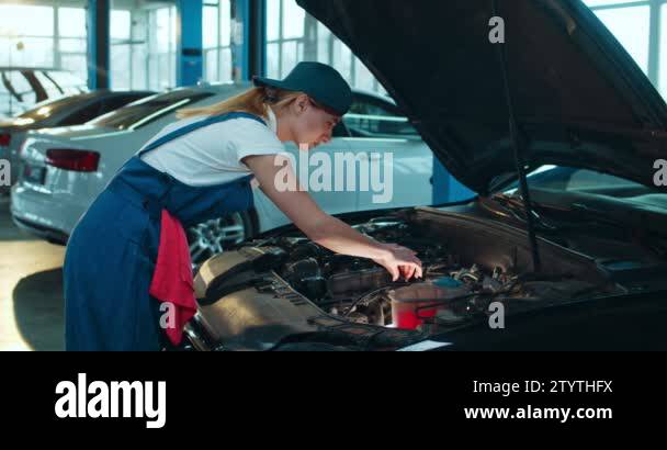 Female Caucasian young auto mechanic standing at open car and repairing ...