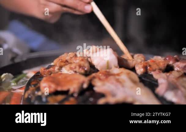 People using chopstick to cooking pick up and flip pork and meet of Korean BBQ barbecue on the ...