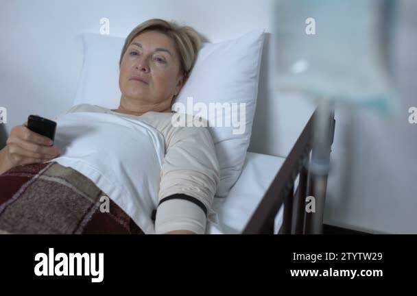 Weak aged woman patient watching TV at hospital ward, falling asleep in ...