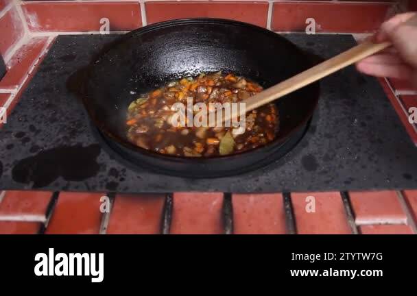 human hand stir boiling oil with meat and spices with a wooden paddle ...