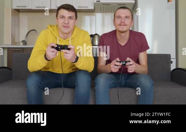 Two young guys playing a video game at home on the couch against the ...