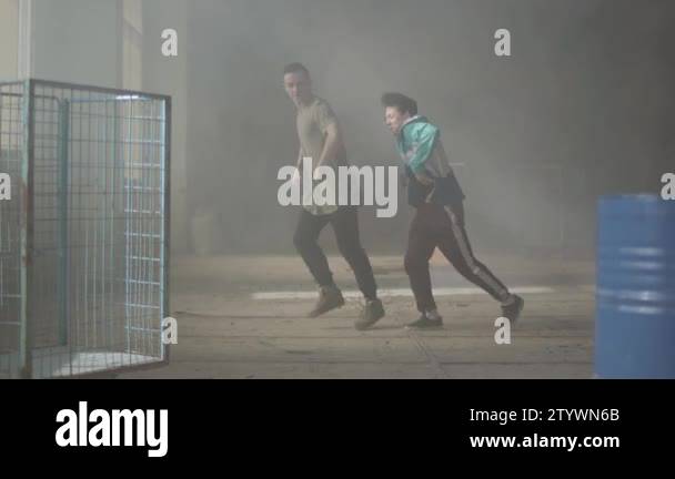 Two skillful young friends dancers dancing in the dark and dusty room ...
