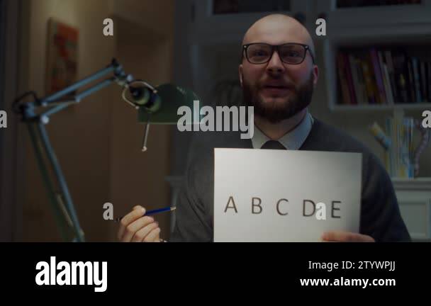 Bearded 30s man in glasses showing sheet of paper with alphabet letters ...
