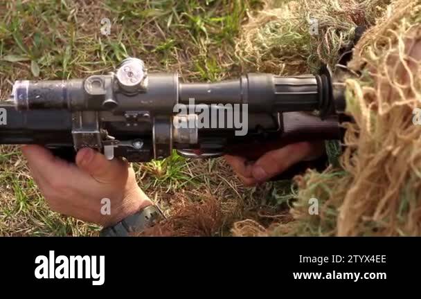A sniper in a masking sniper suit fires a shot from a sniper rifle with ...