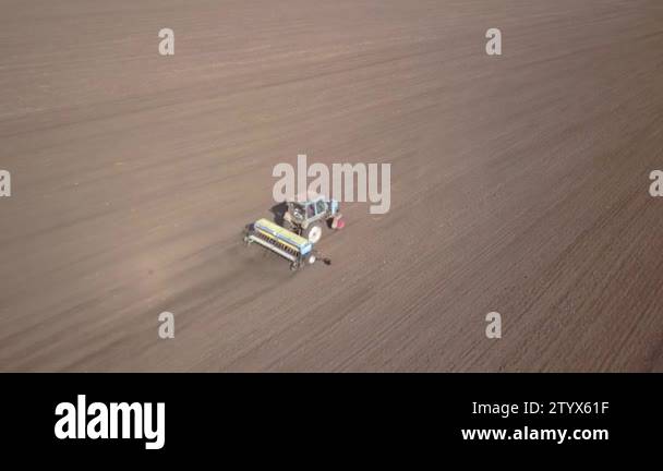 Top down aerial view of green tractor cultivating ground and seeding a ...