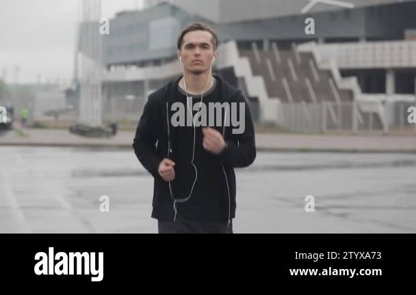 Attractive young man running outdoors wearing earphones slow motion. He ...