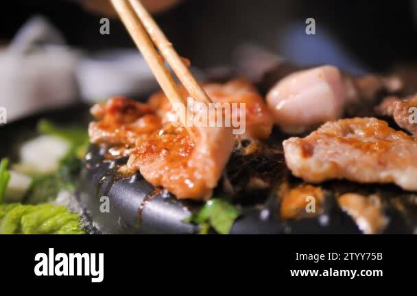 People using chopstick to cooking pick up and flip pork and meet of Korean BBQ barbecue on the ...
