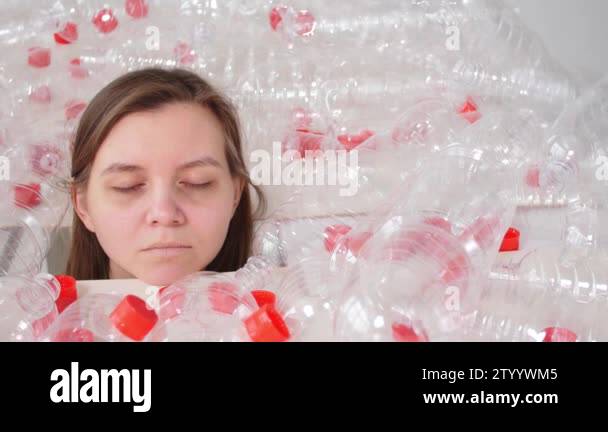Dehydrated sick woman is lying in a pile of plastic bottles ...