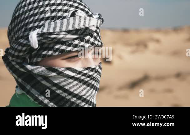 Brave boy in shemagh standing and looking aside in a dry desert on a ...